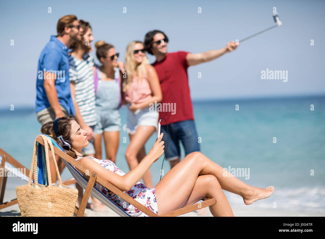 Woman relaxing on deck chair while friends taking selfie at beach ...
