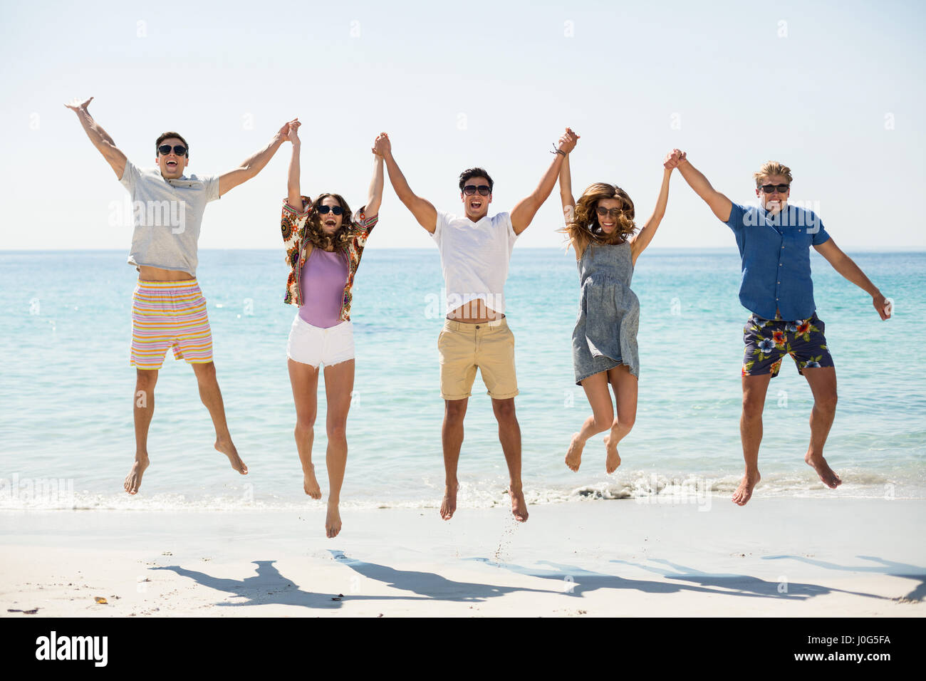 Happy friends jumping with arms raised at beach during sunny day Stock ...