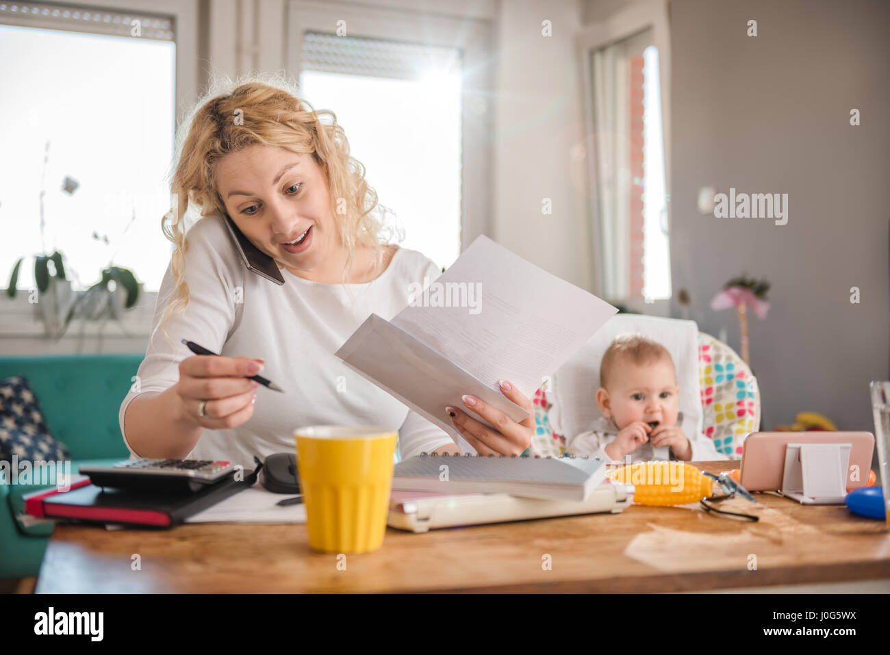 Mother holding letter, writing notes, talking on smart phone at home ...