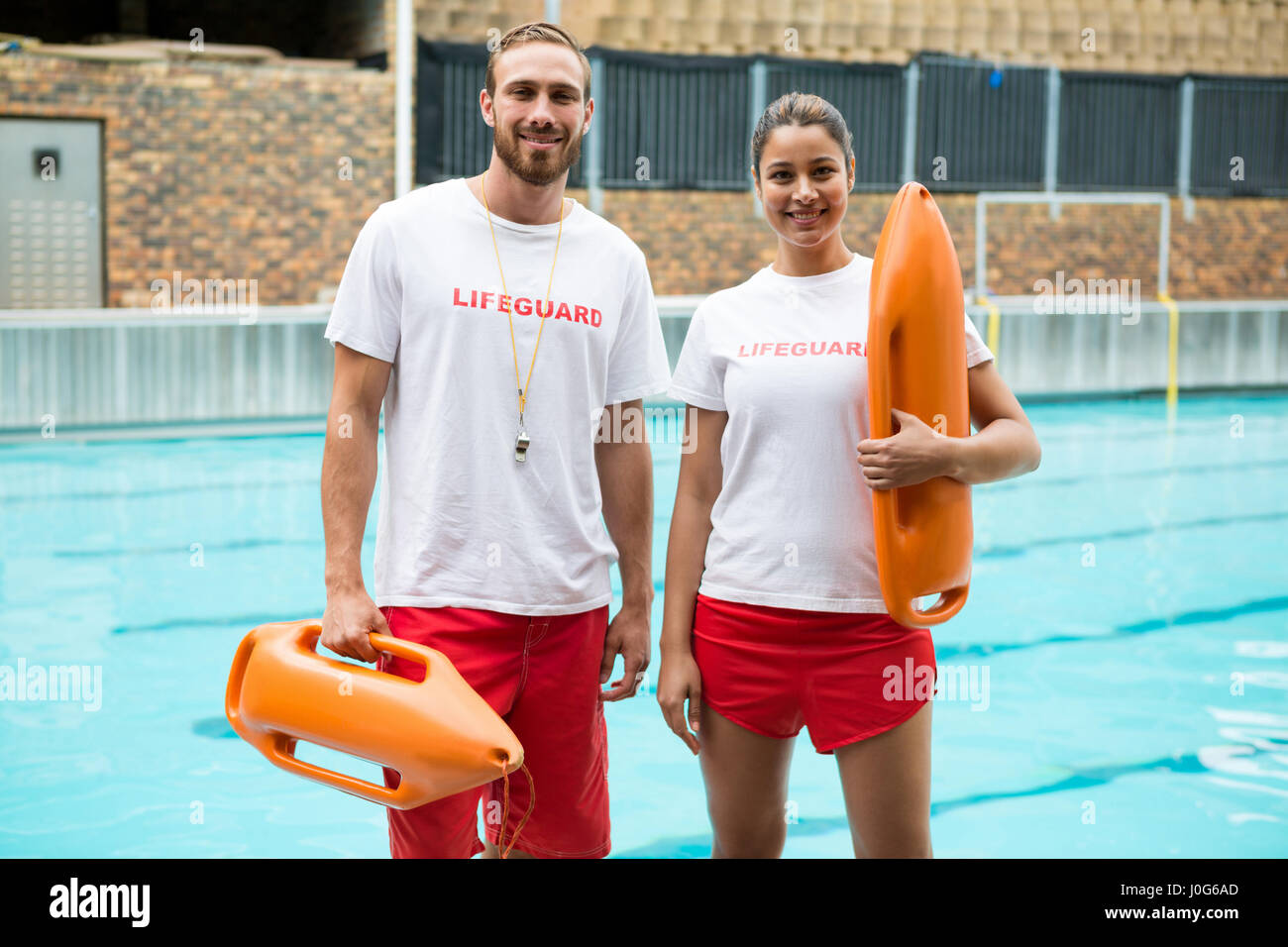 Portrait of two lifeguards standing with rescue buoy at poolside Stock ...