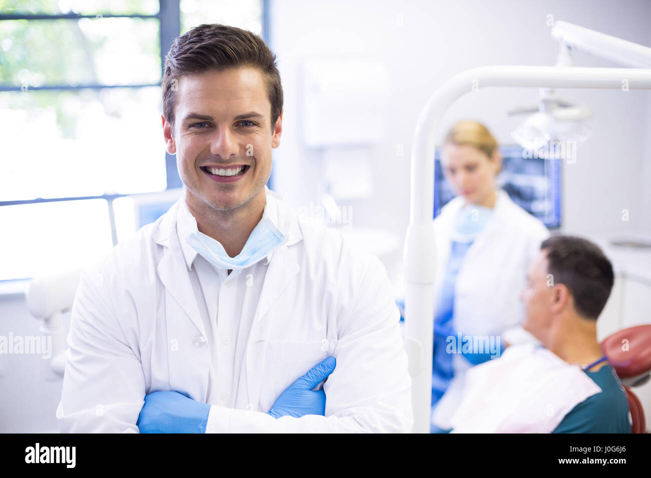 Portrait of dentist standing with arms crossed while his colleague ...