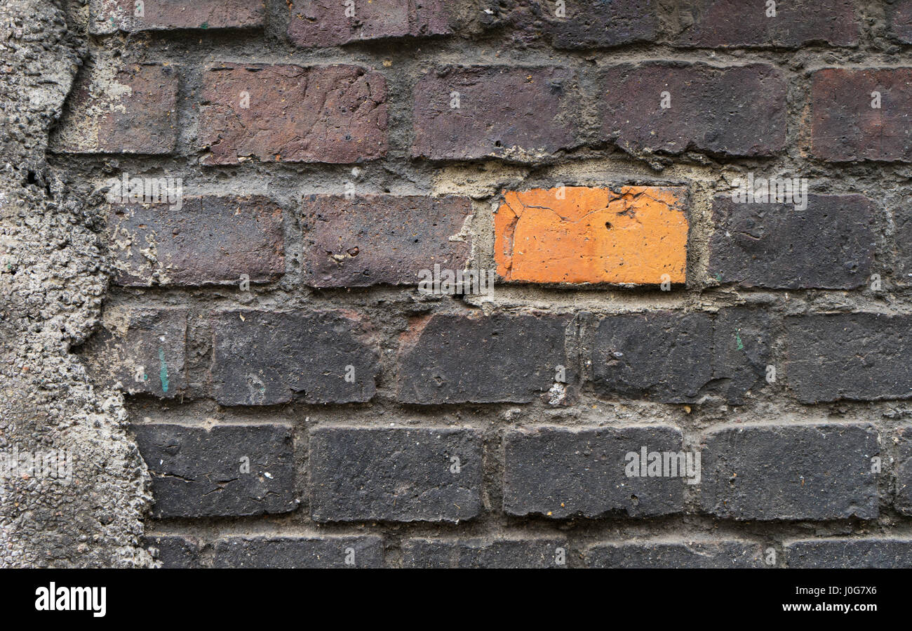 Wall with many dark bricks and a red brick Stock Photo - Alamy
