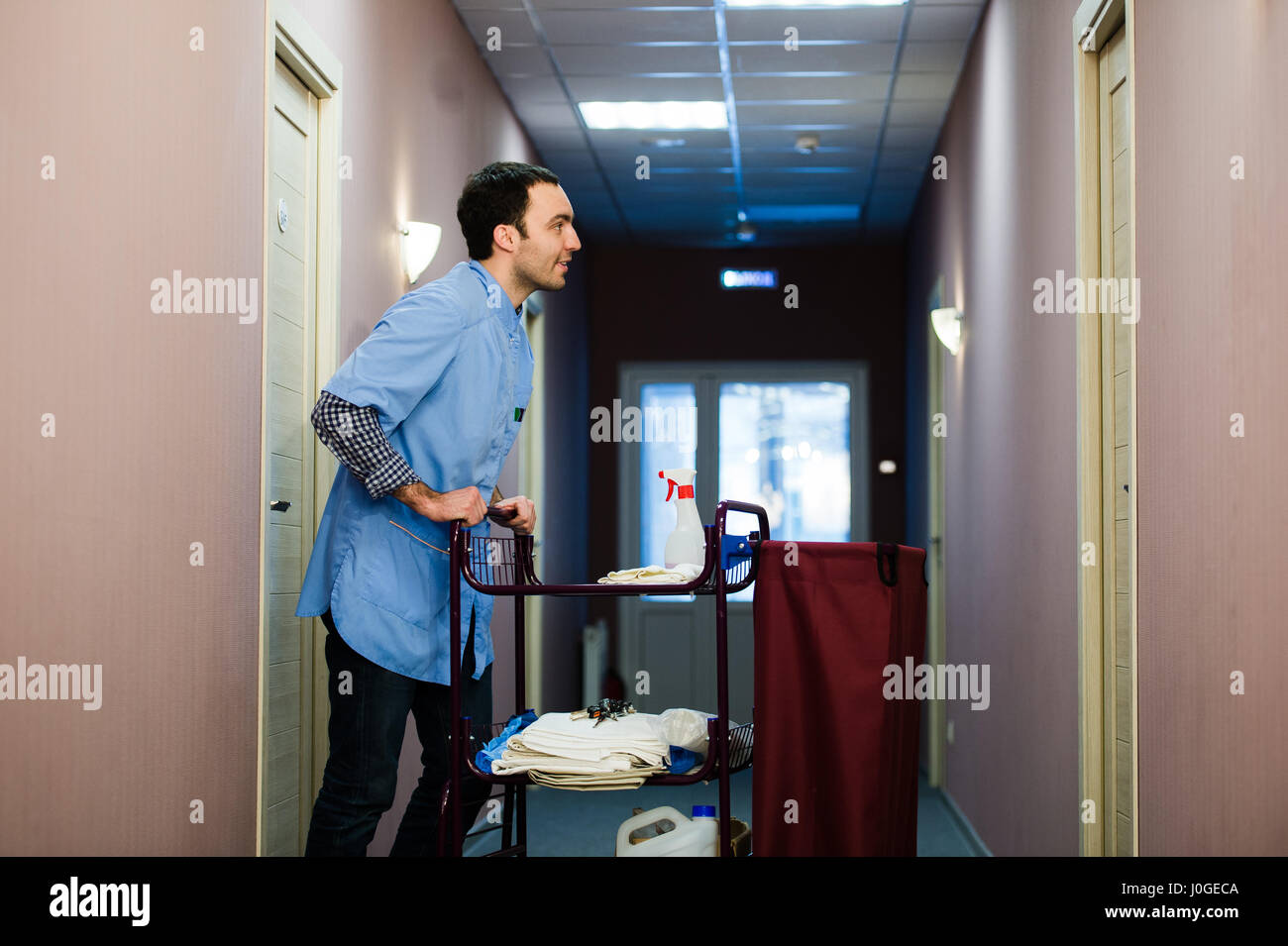 Young man pushing a housekeeping cart laden with clean towels, laundry ...
