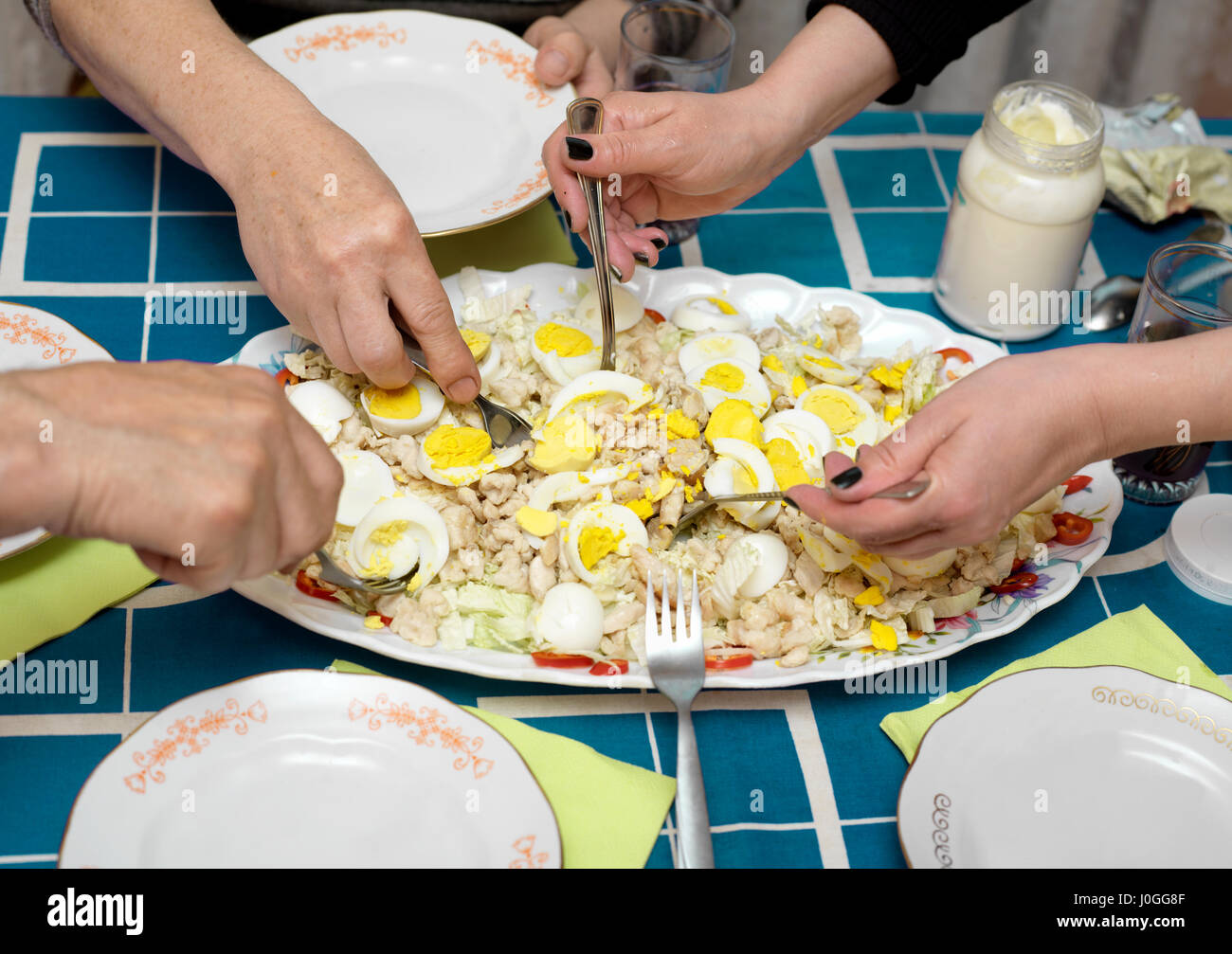 Hands with forks picking food from a large plate in a center of a table ...