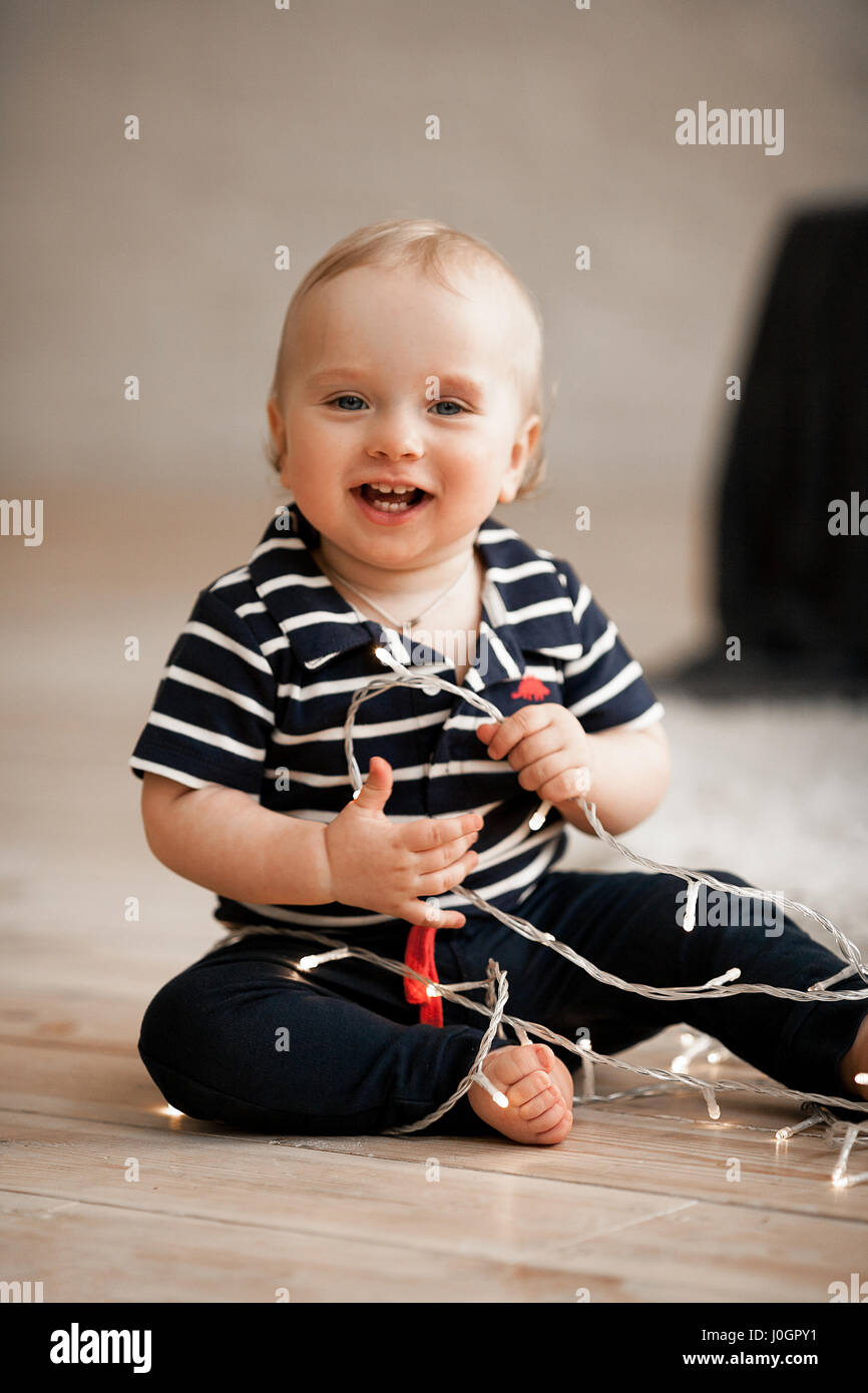 Small baby sits on wooden floor and plays with garland of light bulbs ...