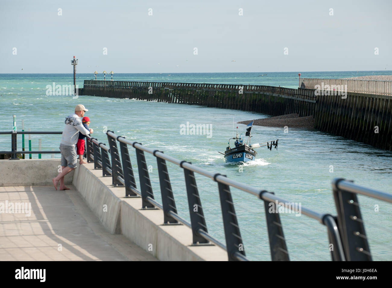 A man and boy watch as a fishing boat returns to the harbour in ...