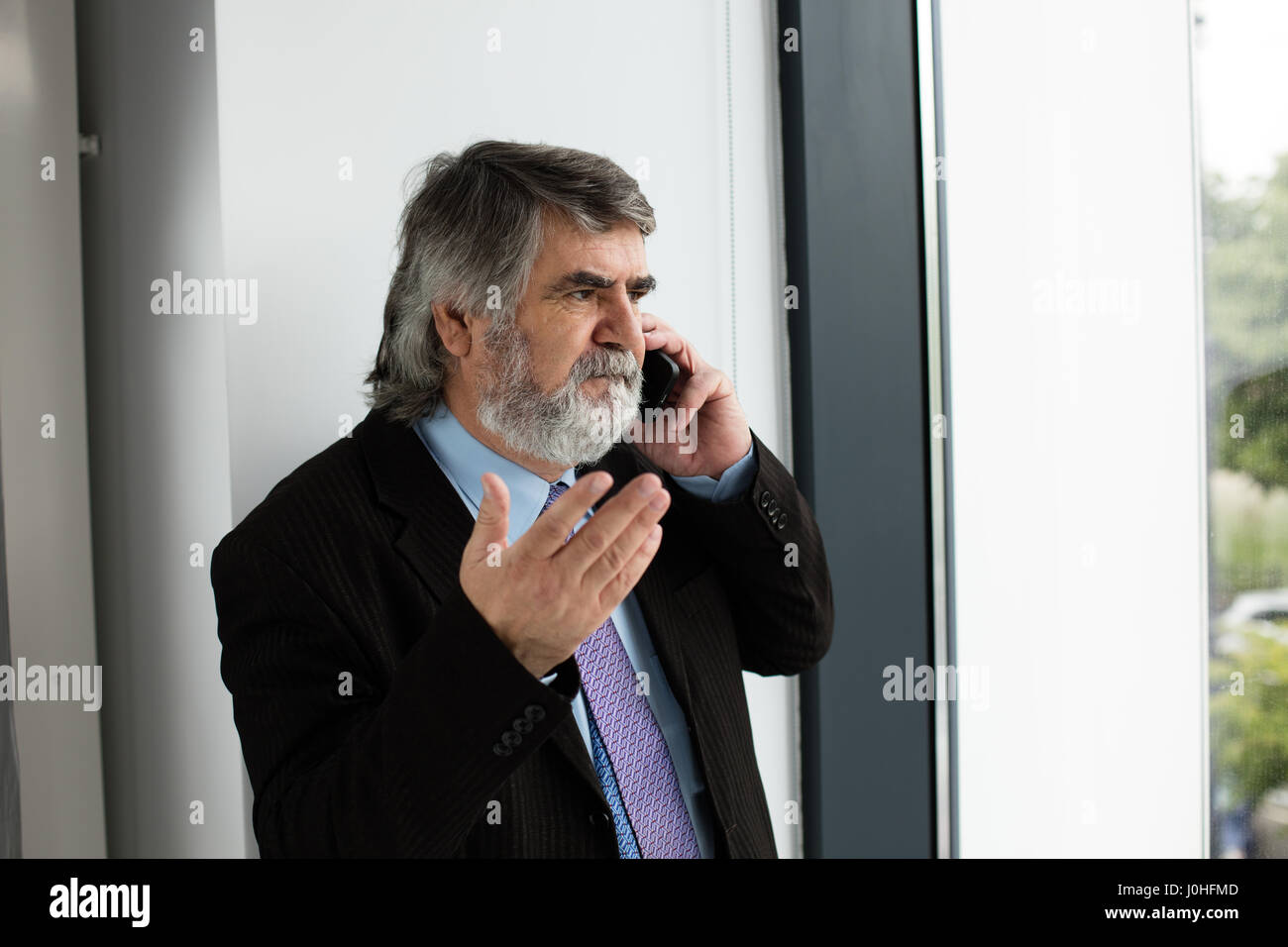 elegant old men having a conversation at cellphone next to a window ...