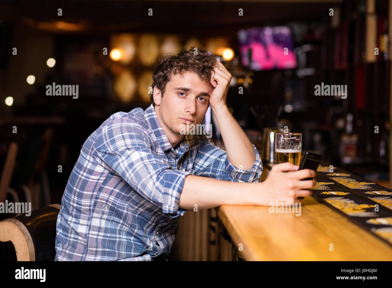 sad single man drinking beer at bar or pub, using his cellphone ...