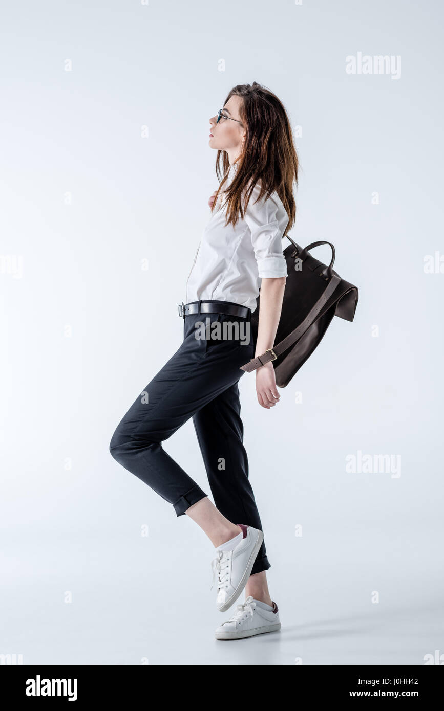 Side view of stylish young woman with leather backpack posing on grey ...