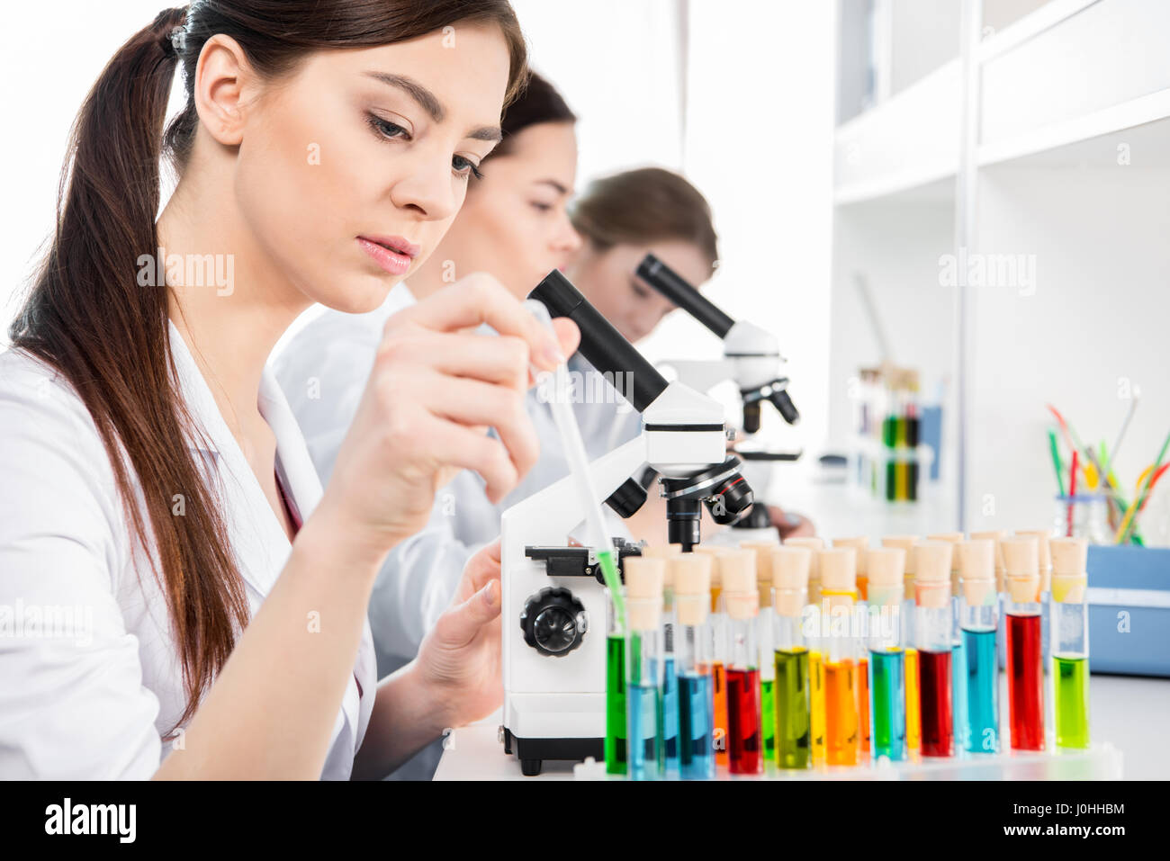Young female scientists working with microscopes and test tubes in ...
