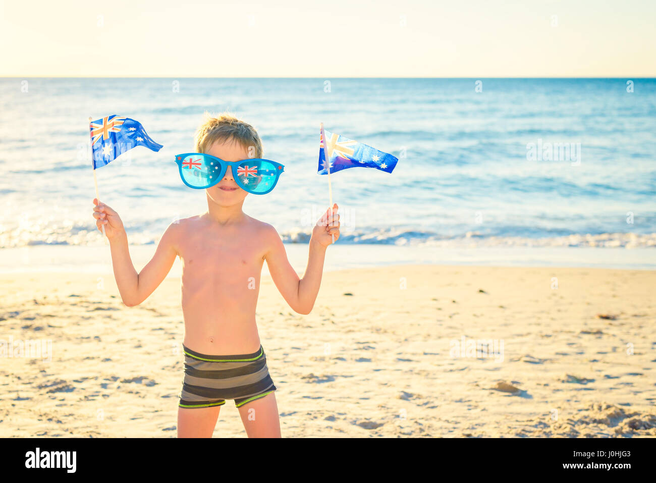 Cute smiling boy standing on the beach and holding Australian flags on ...