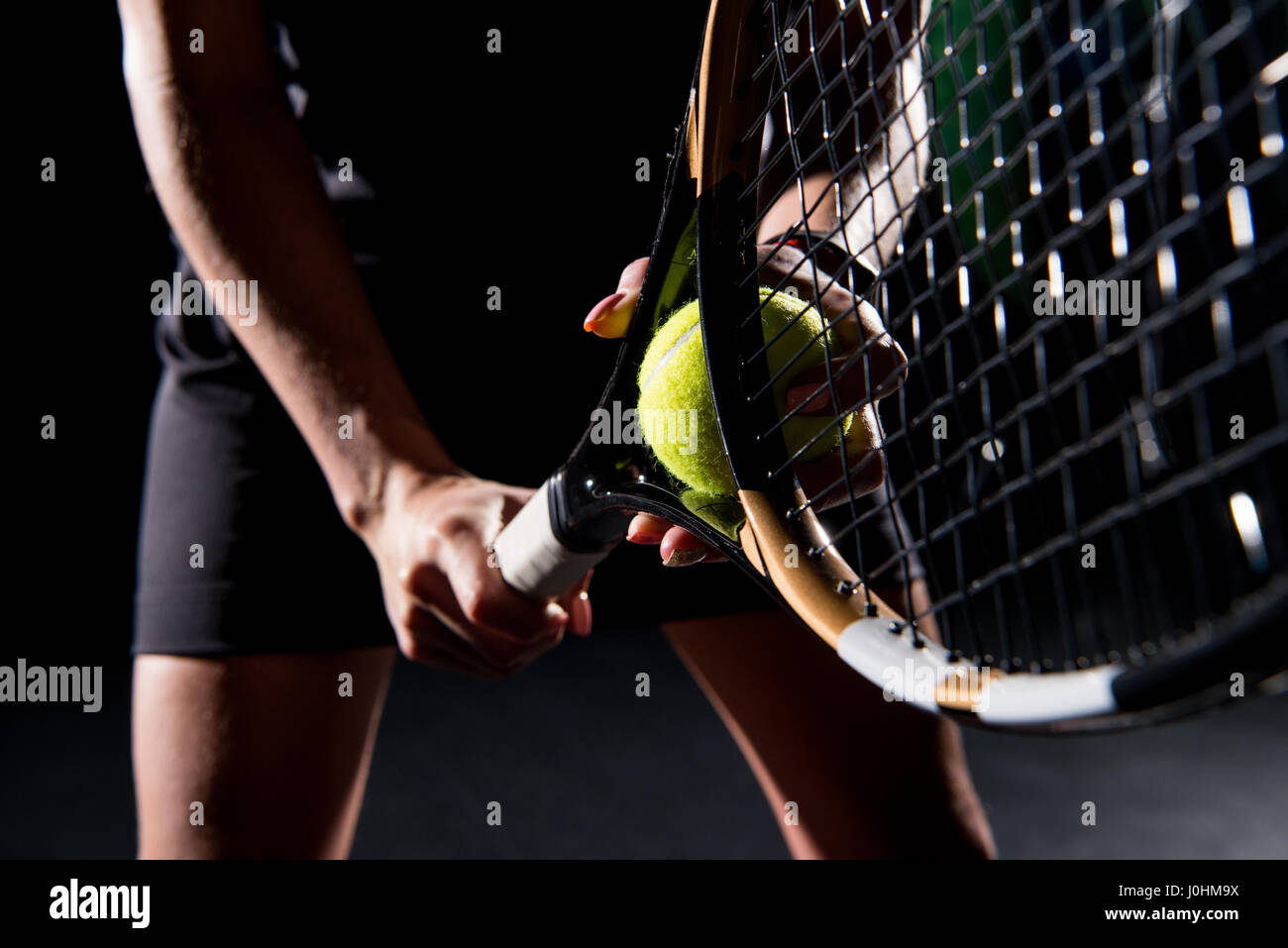 Midsection view of young woman holding tennis racket and ball on black ...