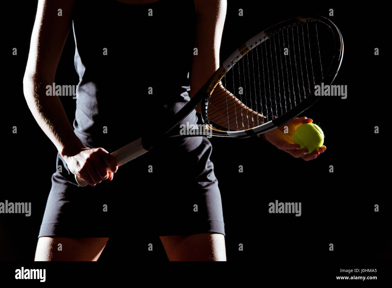 Midsection view of young woman holding tennis racket and ball on black ...