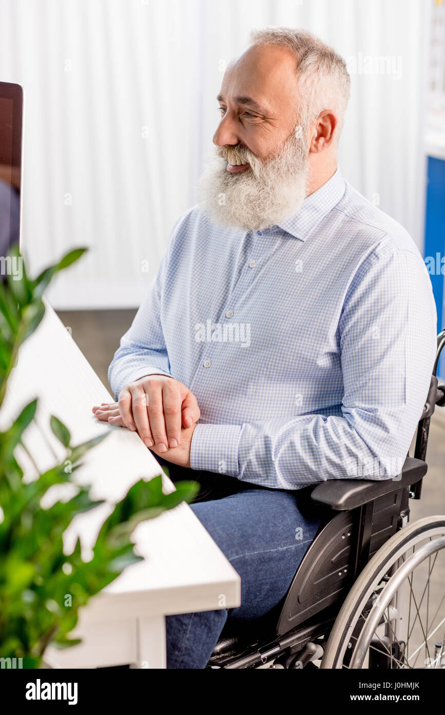 Bearded senior male patient in wheelchair smiling and looking away ...