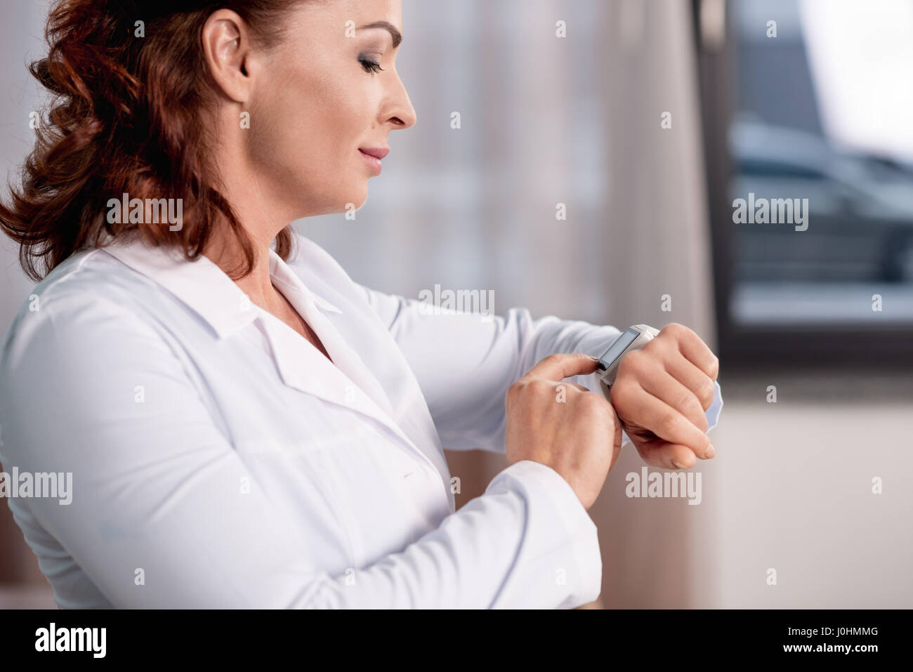 Side view portrait of smiling female doctor using smartwatch in ...