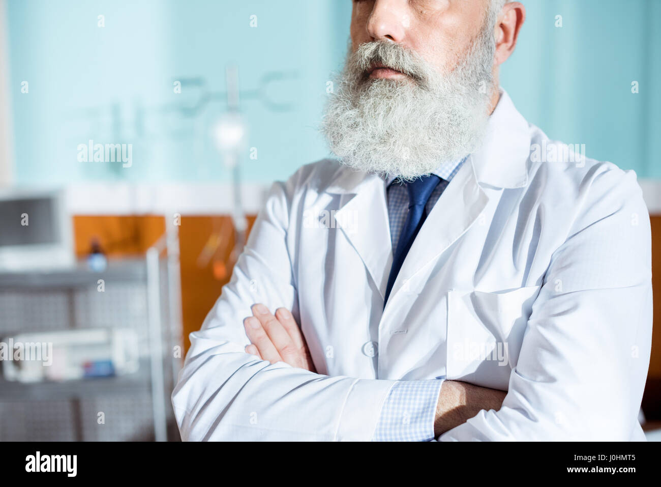 Midsection view of senior bearded doctor standing with hands crossed ...