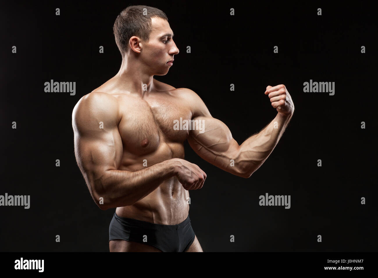 Calm bodybuilder stands in profile against a dark background has big ...