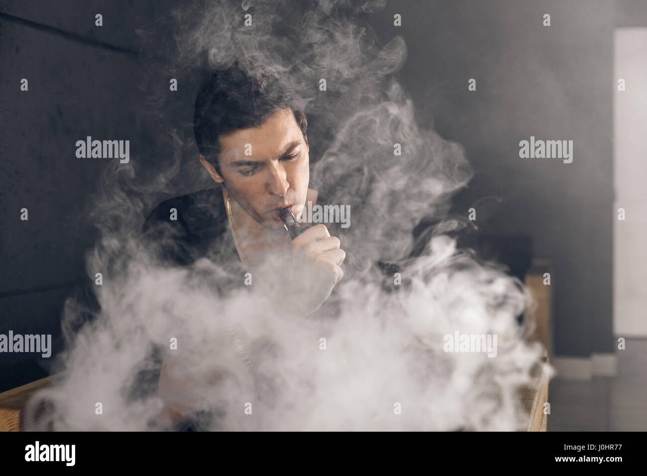 Vaping man holding a mod. A cloud of vapor. Black background. Smoking ...