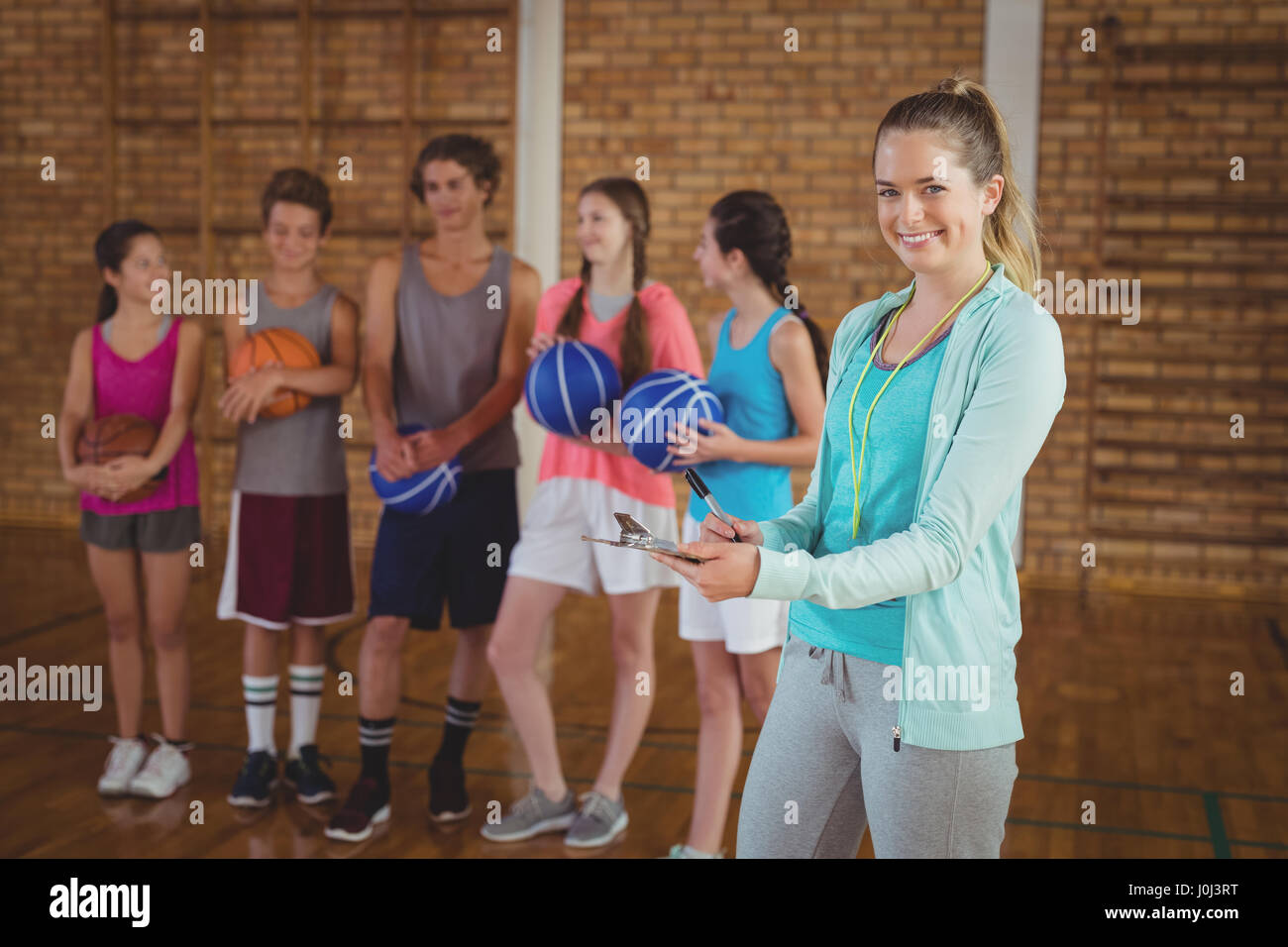 Portrait of smiling coach writing on clipboard in the basketball court ...