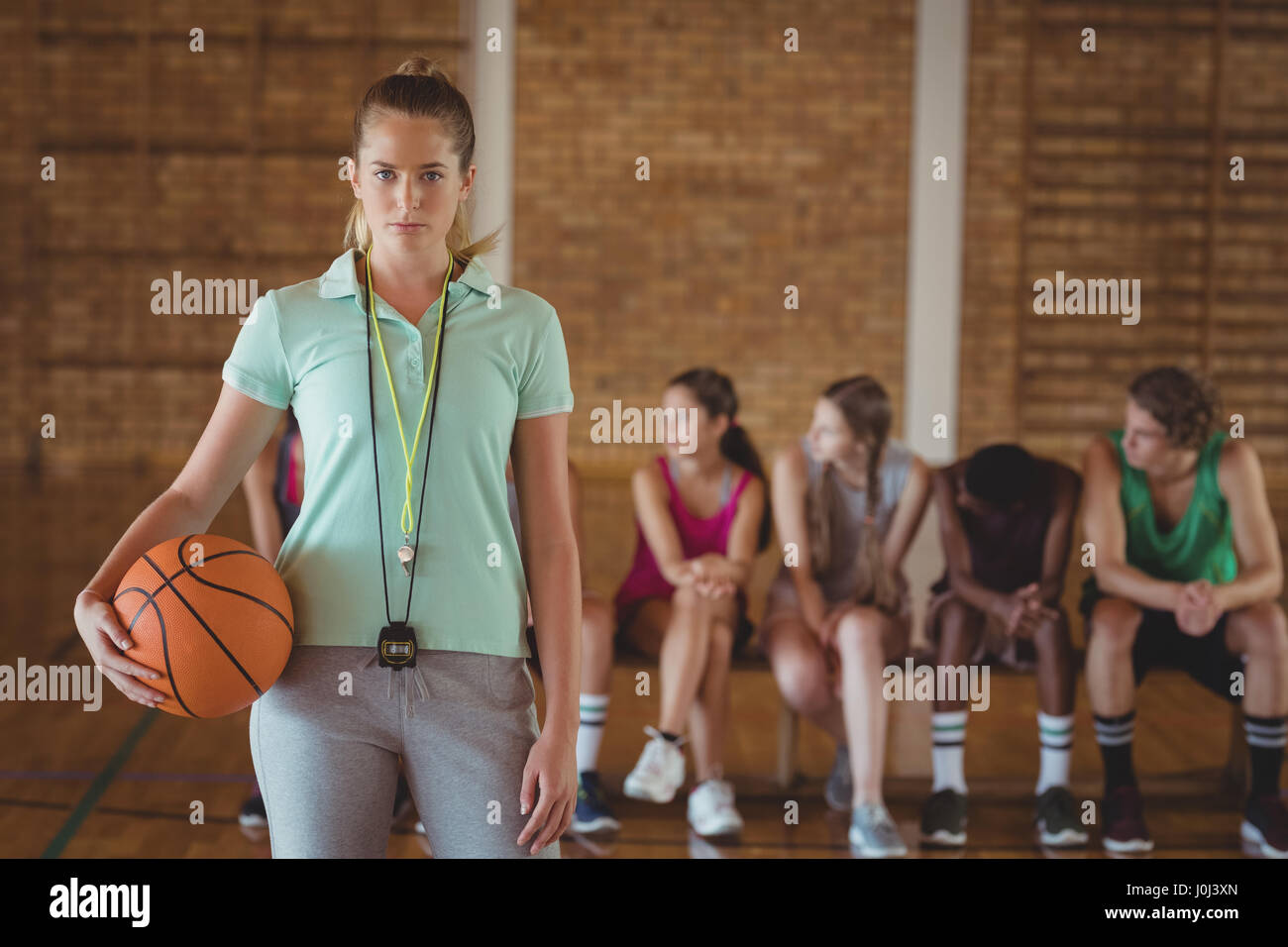 Portrait of female coach standing with basketball in basketball court ...