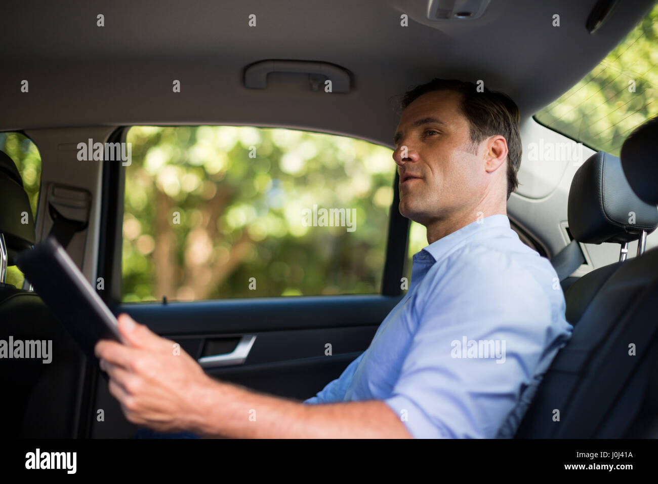 Side view of man holding digital tablet in car Stock Photo - Alamy