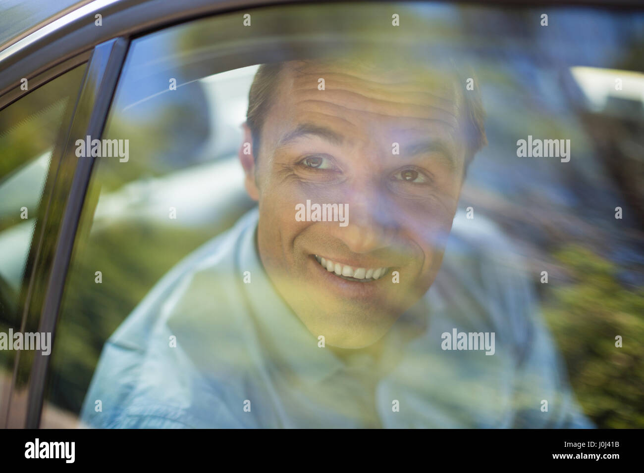 Smiling man looking through car window Stock Photo - Alamy
