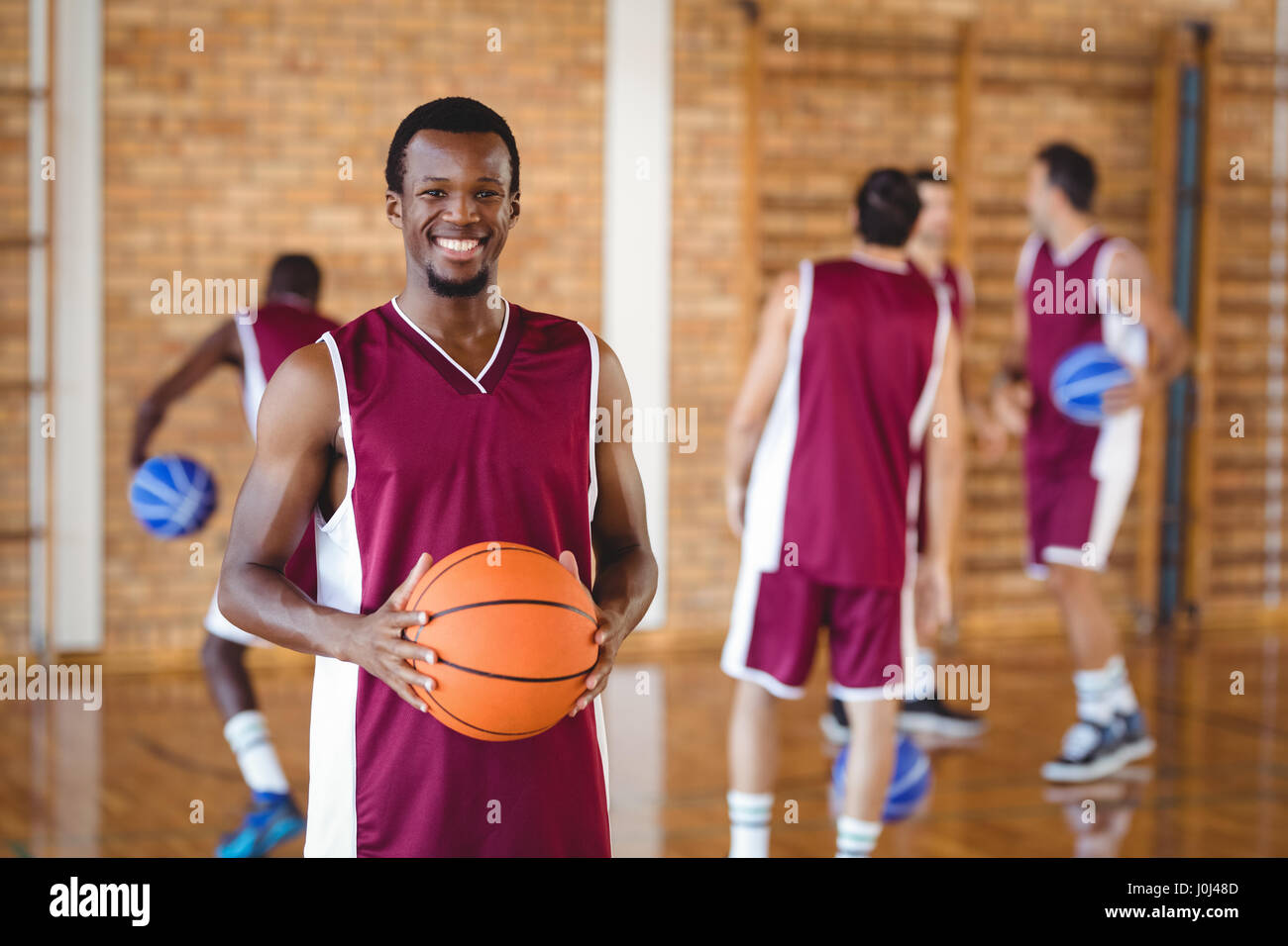 Portrait of smiling basketball player holding a basketball in the court ...