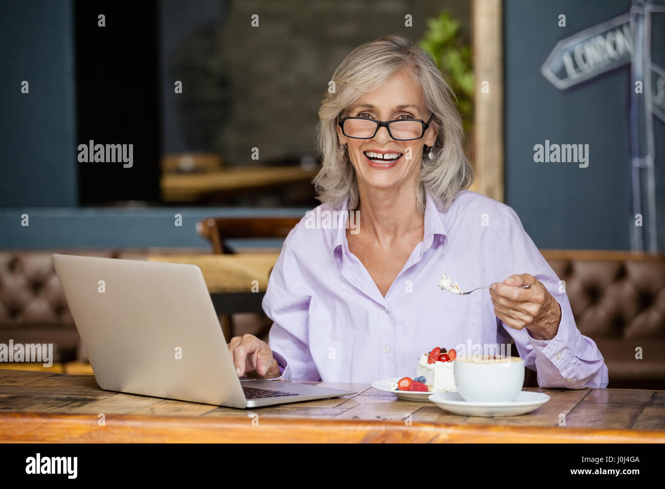 Portrait of senior woman using laptop computer while eating breakfast ...