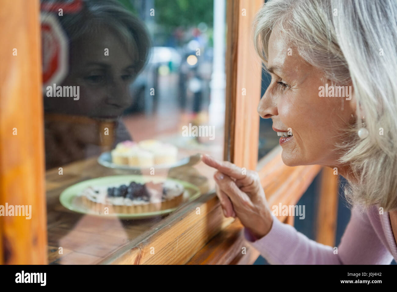 Close up of senior woman looking at food through glass window of coffee ...
