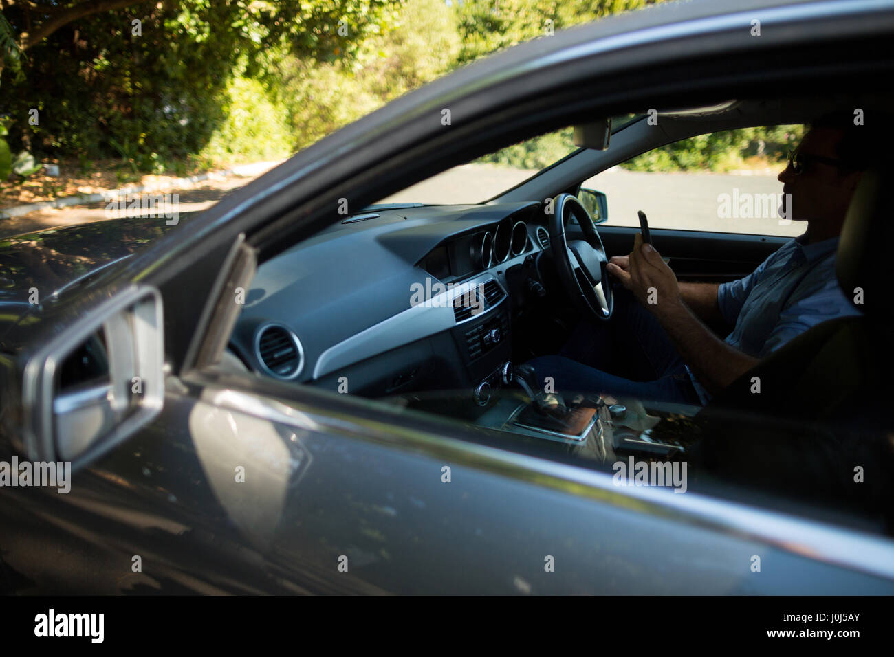 Young man using mobile phone while driving car Stock Photo - Alamy