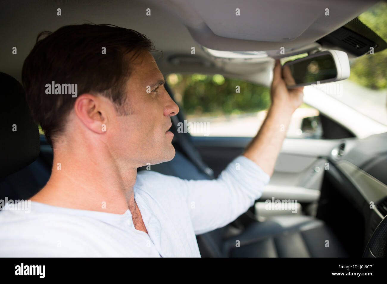 Young man adjusting rearview mirror in car Stock Photo - Alamy