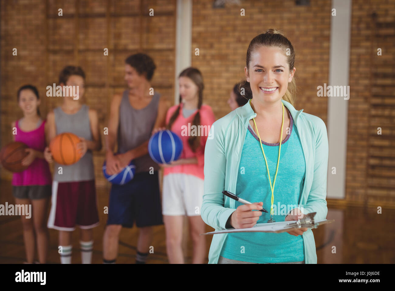 Portrait of smiling coach writing on clipboard in the basketball court ...