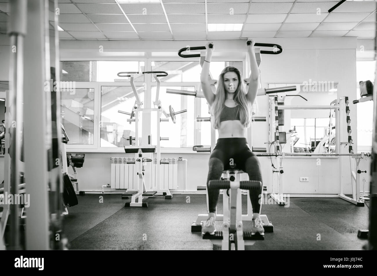 girl in a bright white gym. A blonde woman doing a strength exercise ...