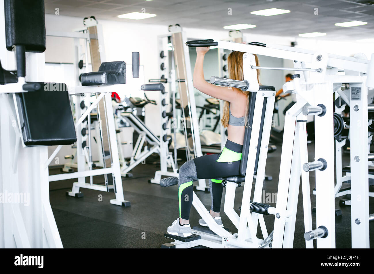 girl in a bright white gym. A blonde woman doing a strength exercise ...
