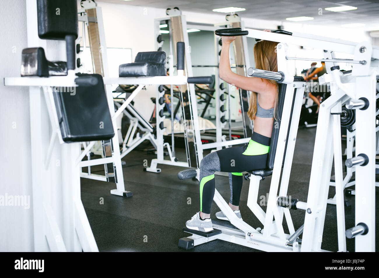 girl in a bright white gym. A blonde woman doing a strength exercise ...