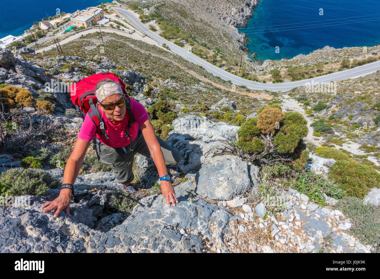 Female scrambling up rocks high above sea and road Stock Photo - Alamy