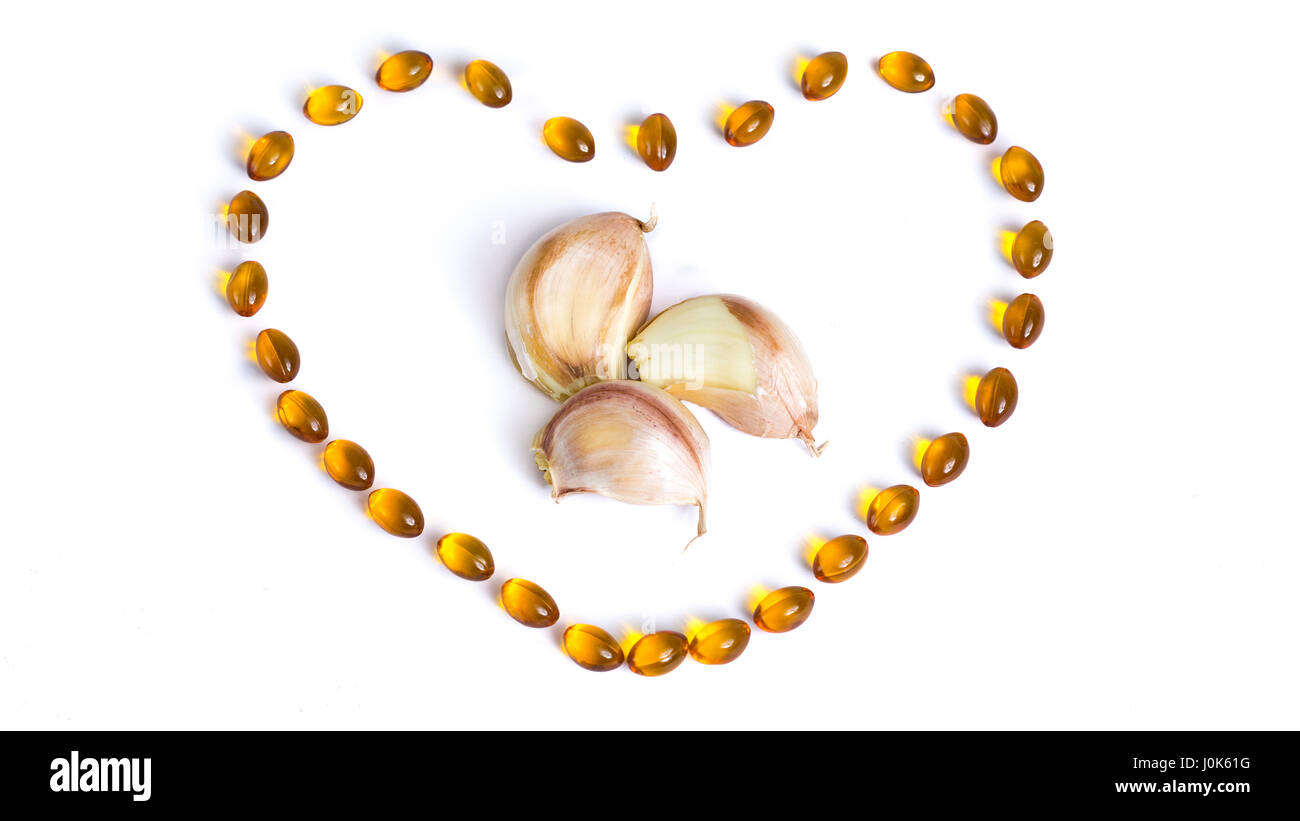 Organic garlic and garlic capsules in heart shape in front of white ...