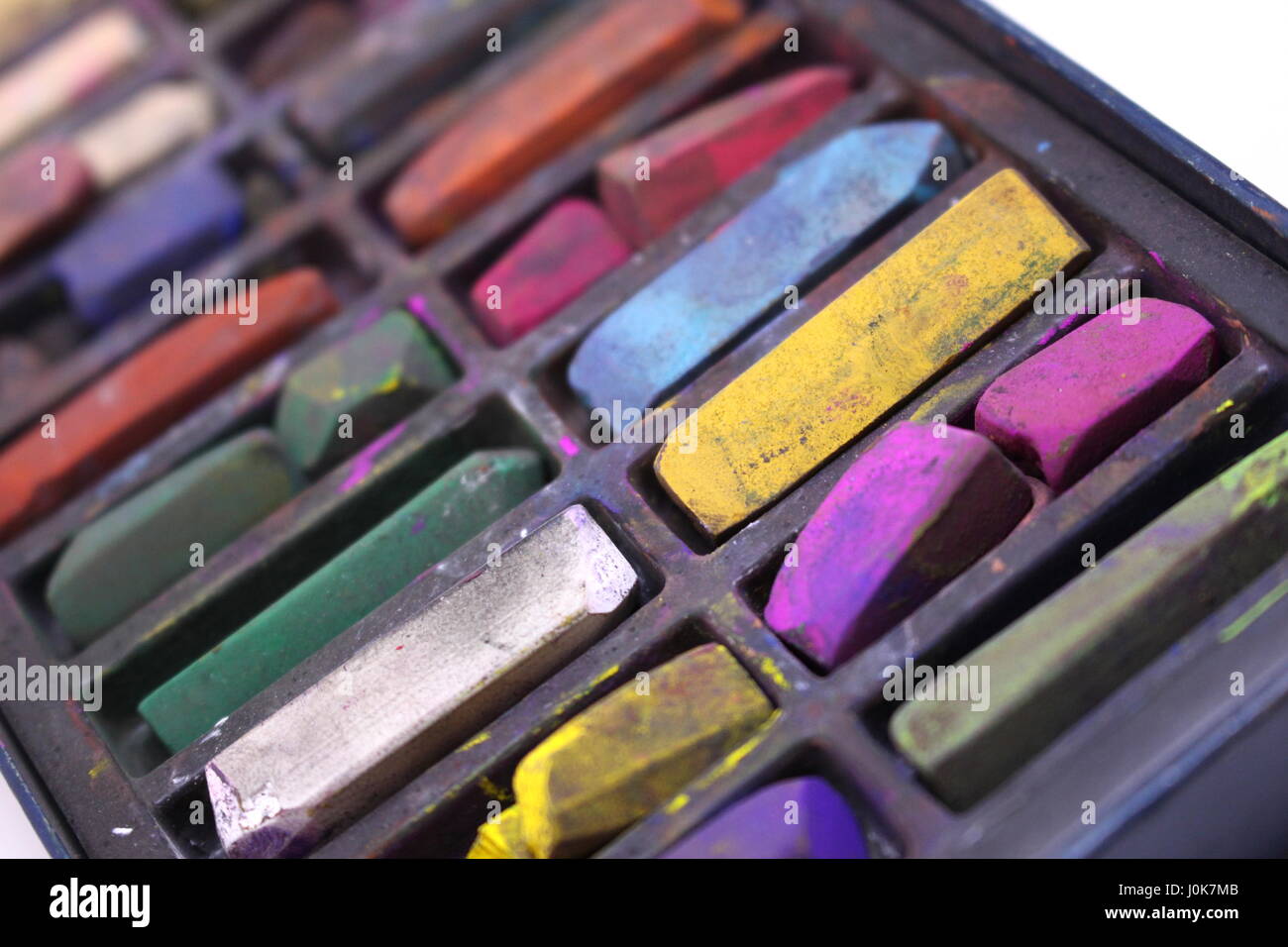 A close up photograph of a box of colorful used chalk pastels, some ...