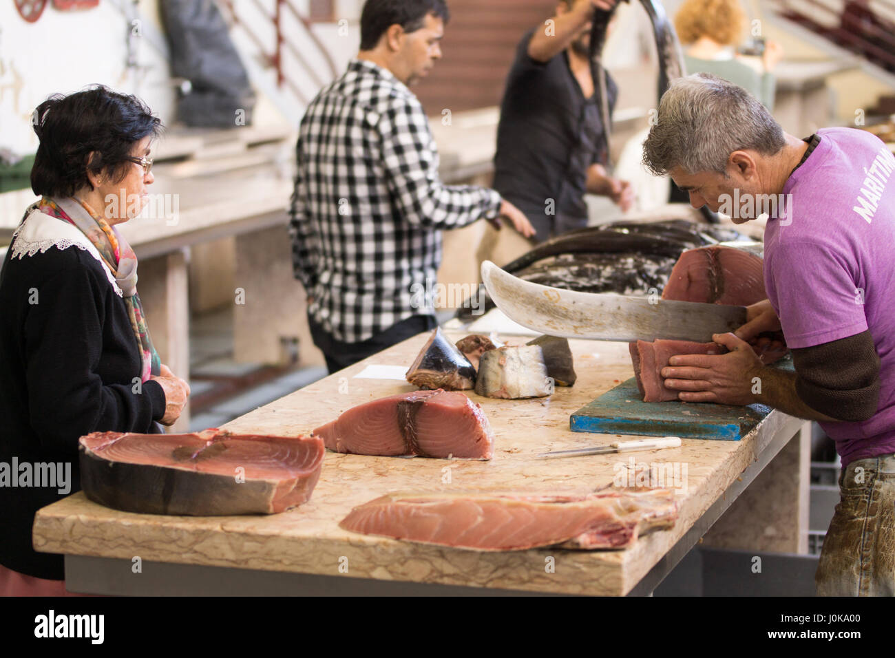 A fishmonger cutting tuna fish steaks for a customer at the Mercardo ...