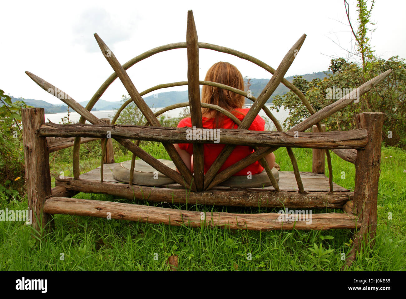 A woman stops to rest on a large wooden bench in the woods on a lake ...