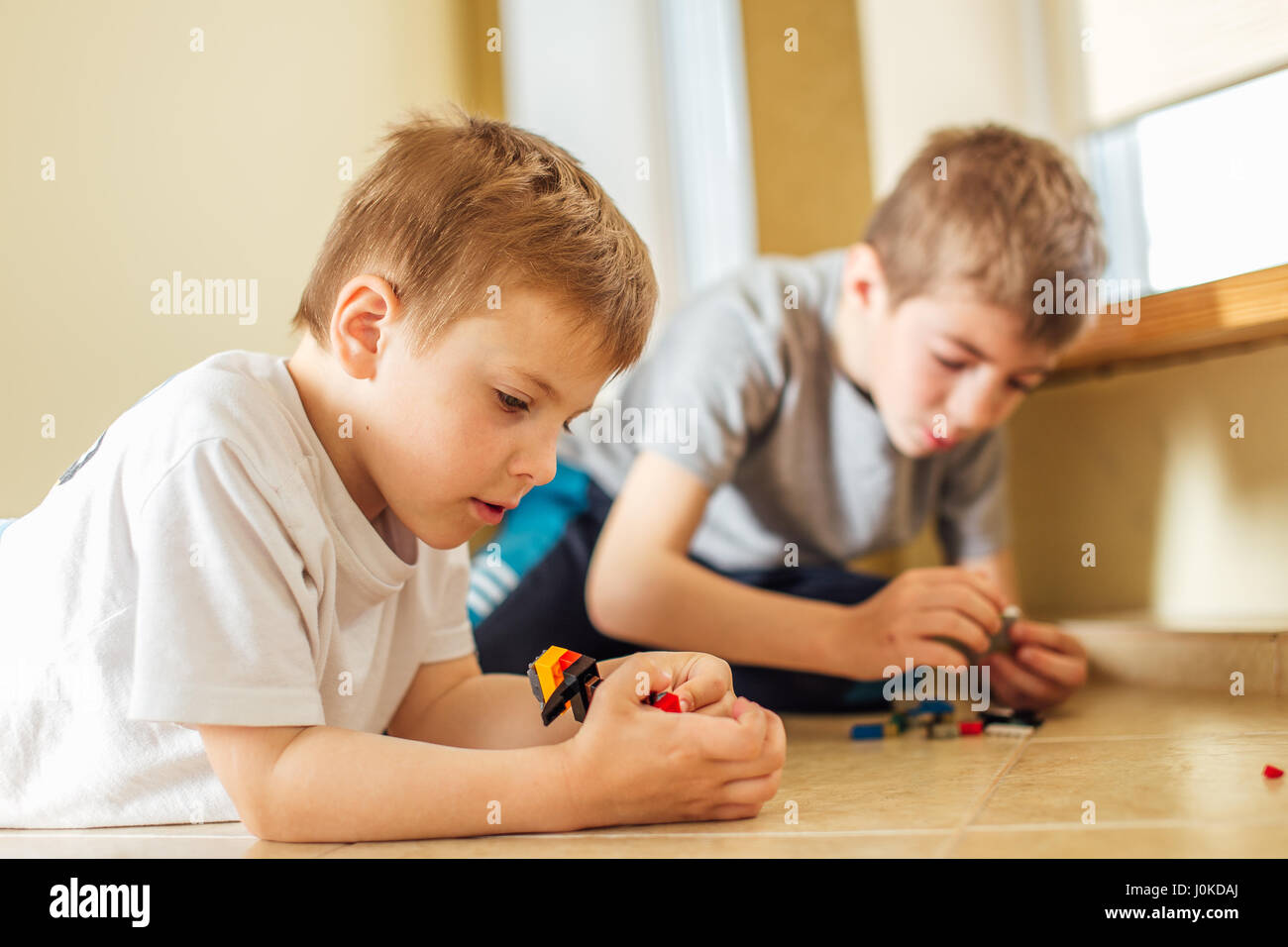 Two boys playing with lego at home with light from window background ...