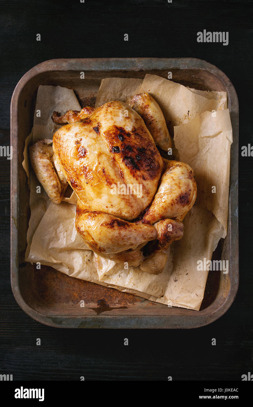 Grilled baked whole organic chicken on backing paper in old oven tray ...