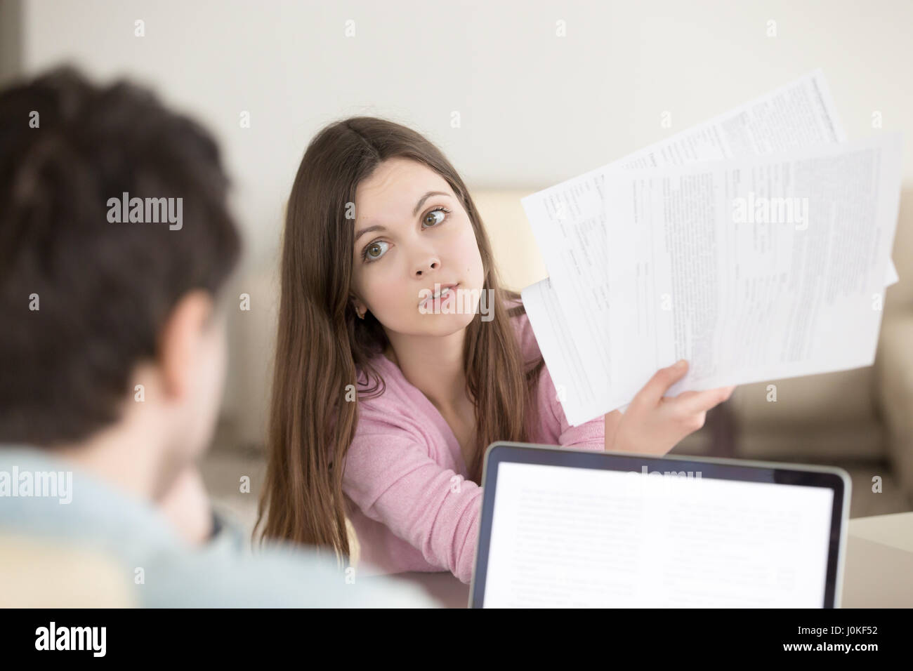 Surprised young woman showing papers to man with questioning loo Stock ...