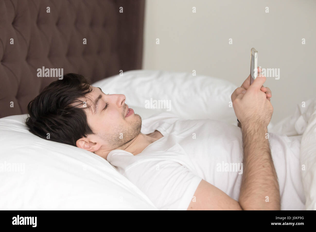 Young man relaxing in bed at home using mobile smartphone Stock Photo ...