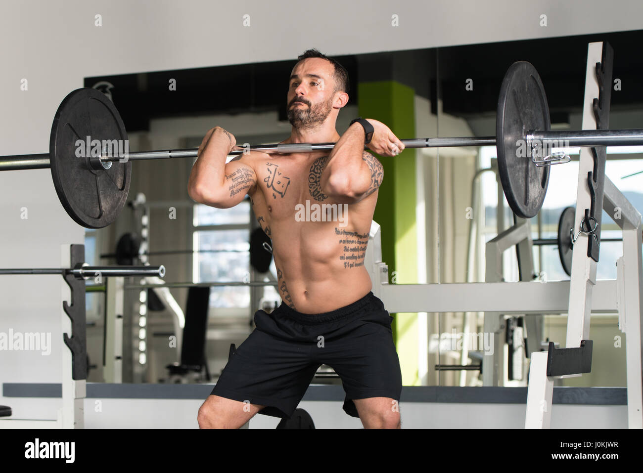 Healthy Fitness Man Working Out Legs With Barbell In A Gym - Front ...