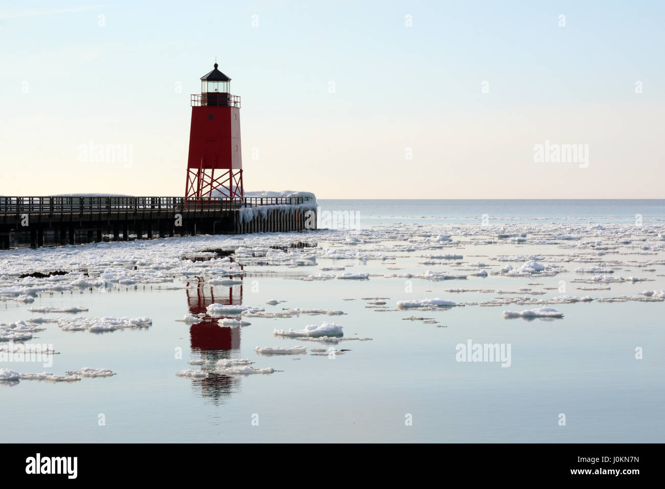 A red lighthouse reflects in the ice dotted water of Lake Michigan on a ...