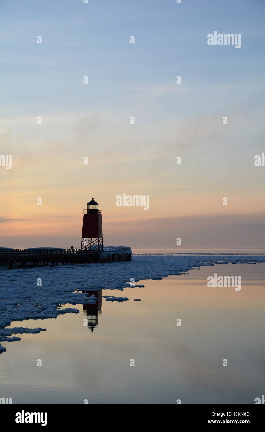 A lighthouse reflects in the calm water of Lake Michigan at sunset in ...