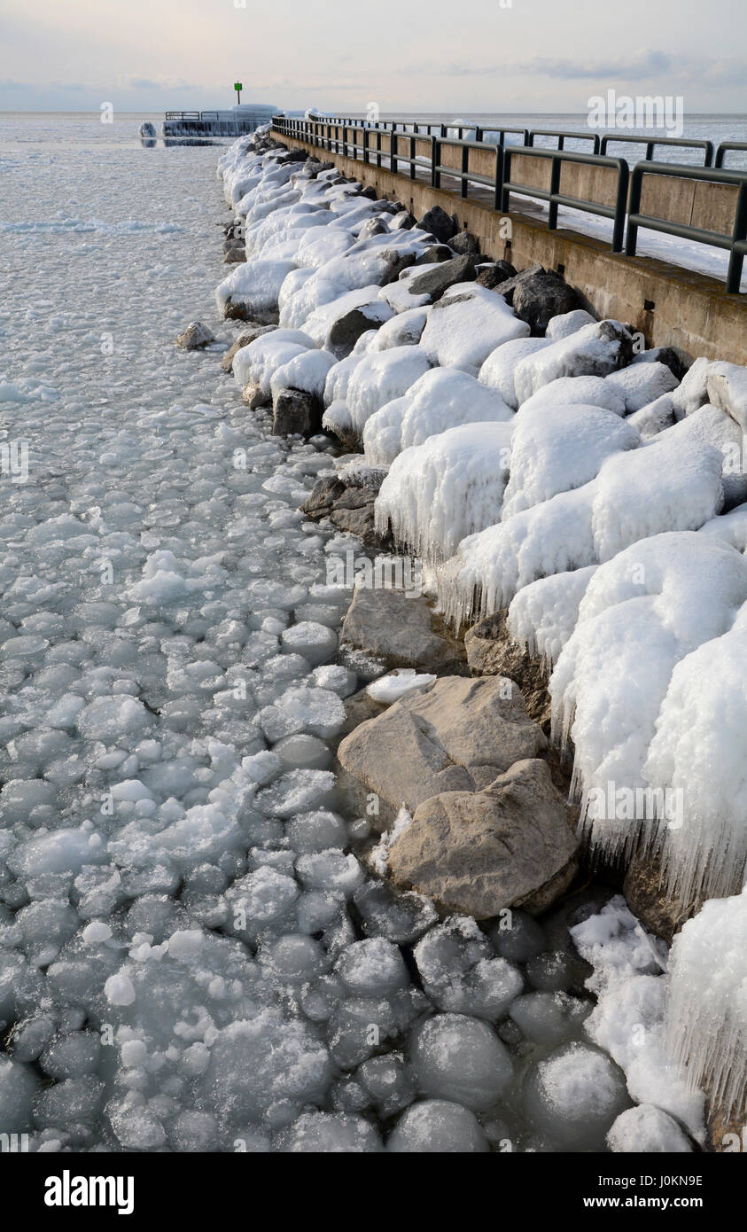 Snow covered rocks and balls of ice line a pier in northern Michigan ...