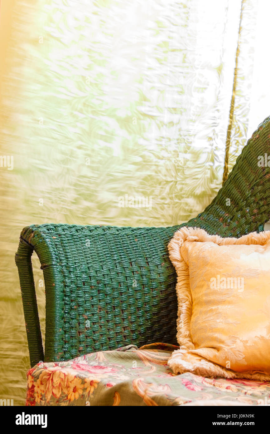 An old green wicker chair sits in front of a windblown curtain with ...