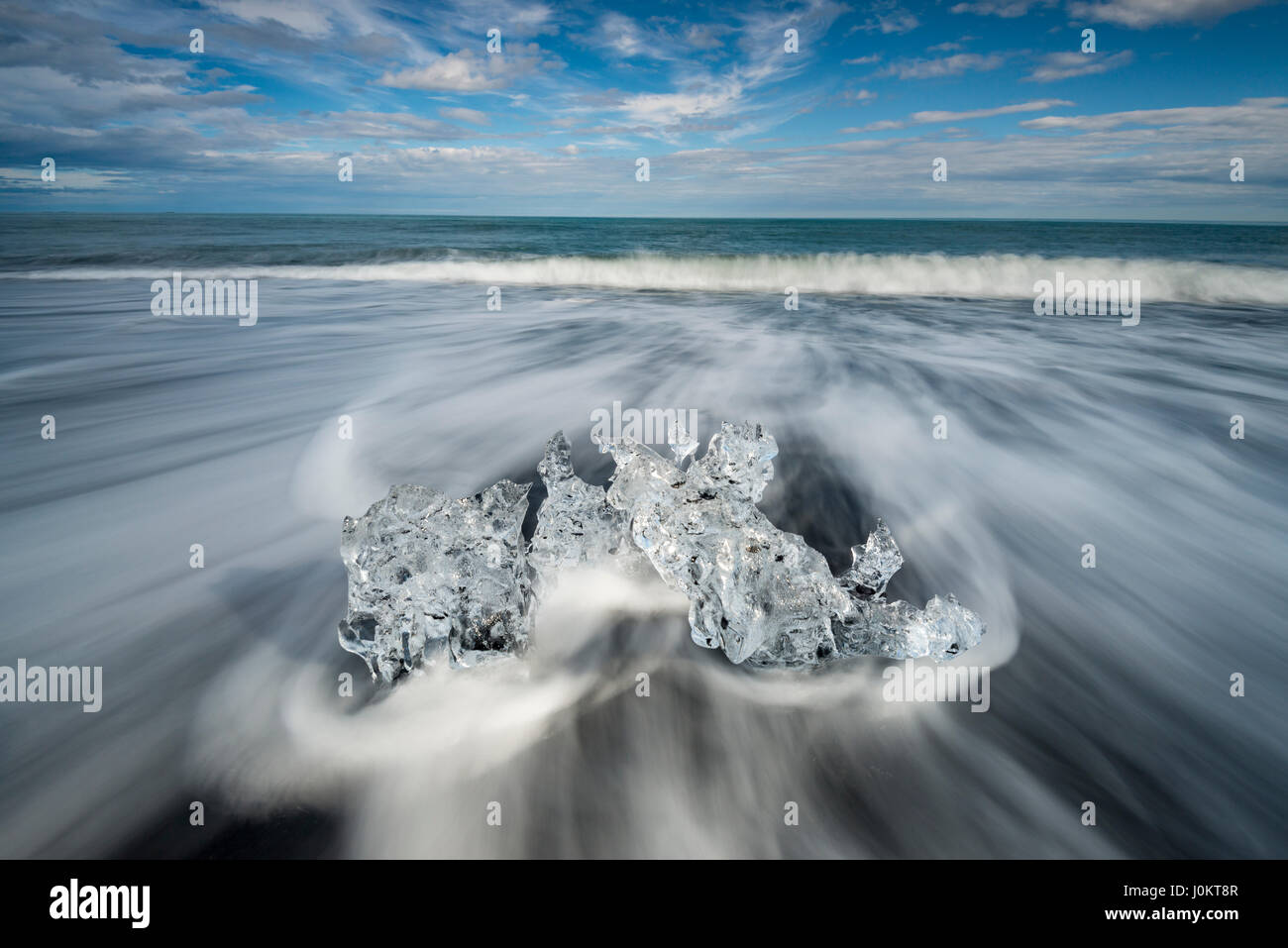 Melting iceberg lying in the surf, black volcanic beach, near ...